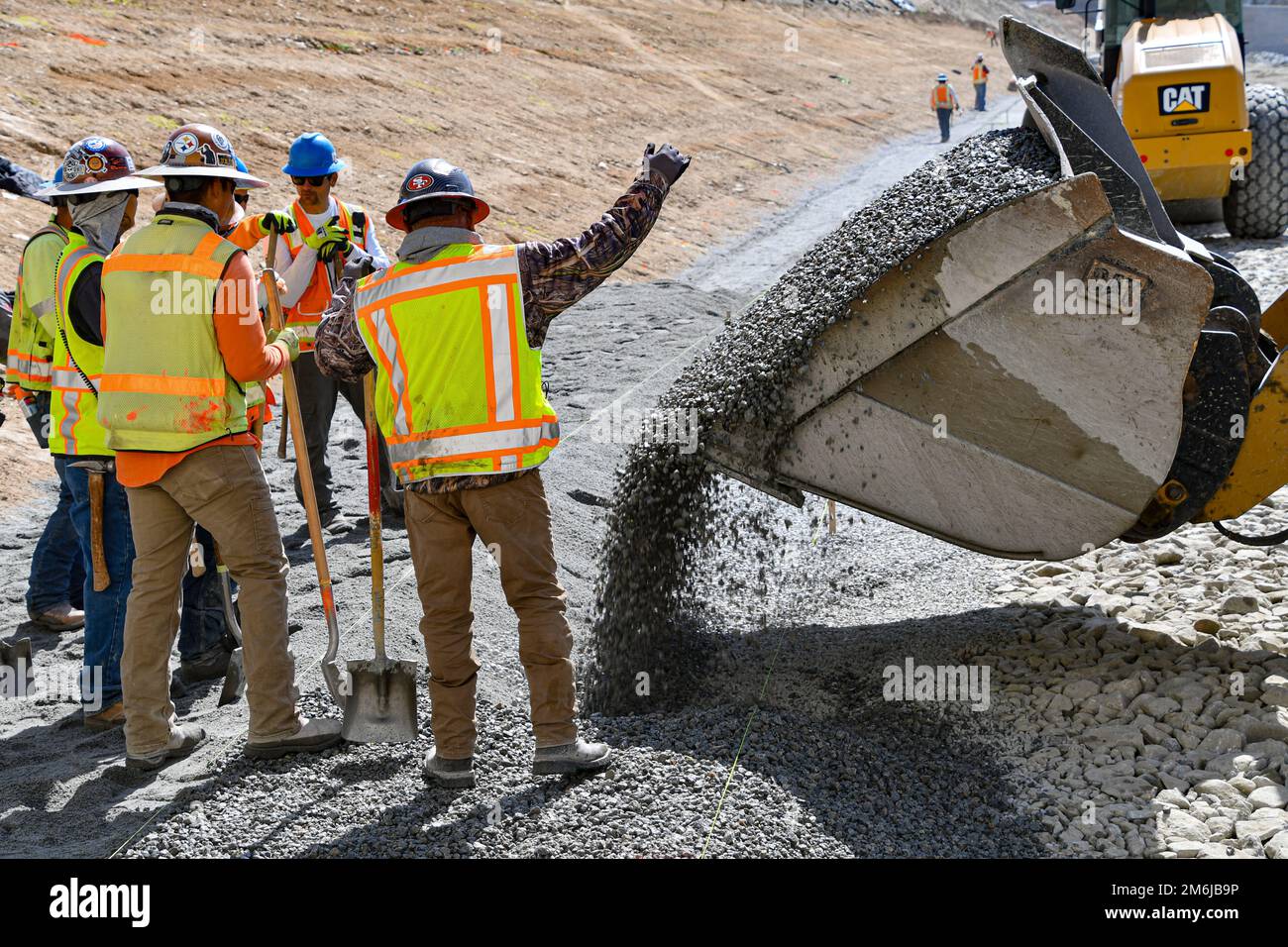 Workers guide a front end loader dumping drain rock on the downstream ...