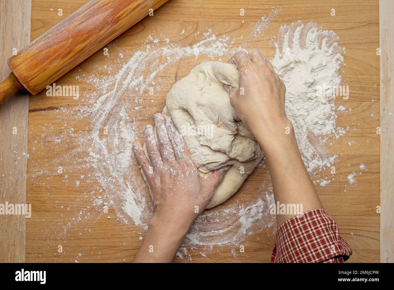 A flatlay photo of the hands of a woman kneading a ball of dough on a ...