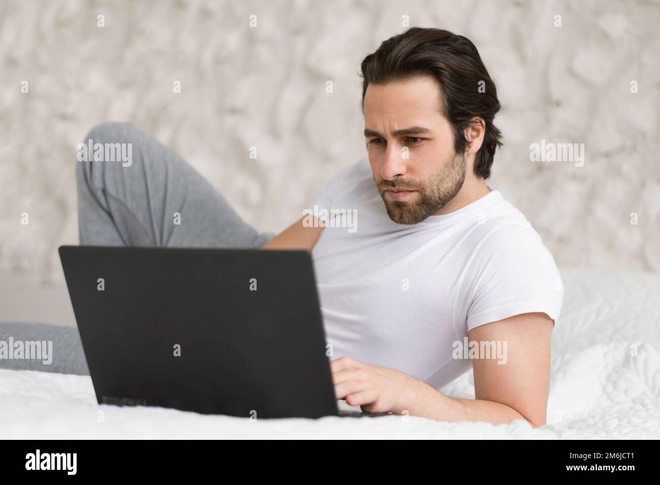 Serious concentrated young caucasian guy lying on bed, watching video ...