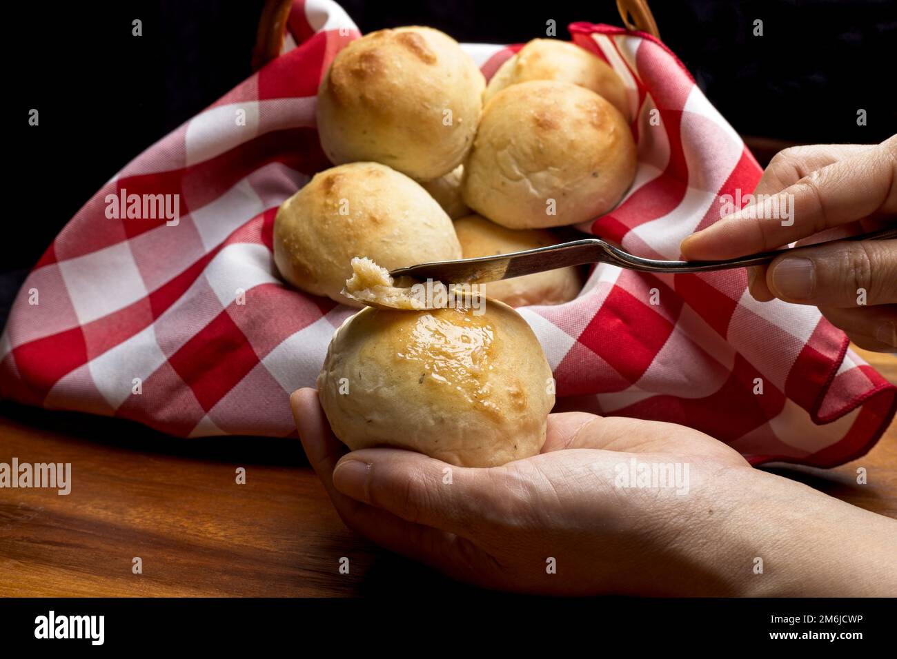 A close up photo of hands holding a roll and spreading butter over the ...