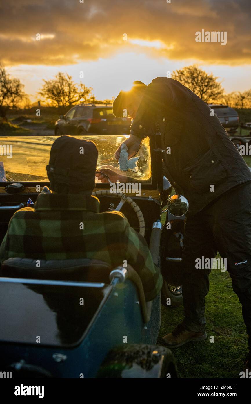 Male wiping clean the front wind screen of an open top pre war austin 7 ...
