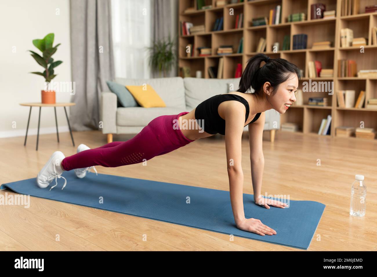 Young asian lady doing domestic training on yoga mat, standing in plank ...