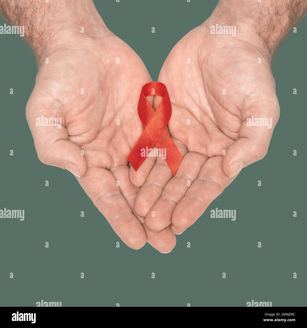 Red awareness ribbon bow on mans helping hands isolated on green ...