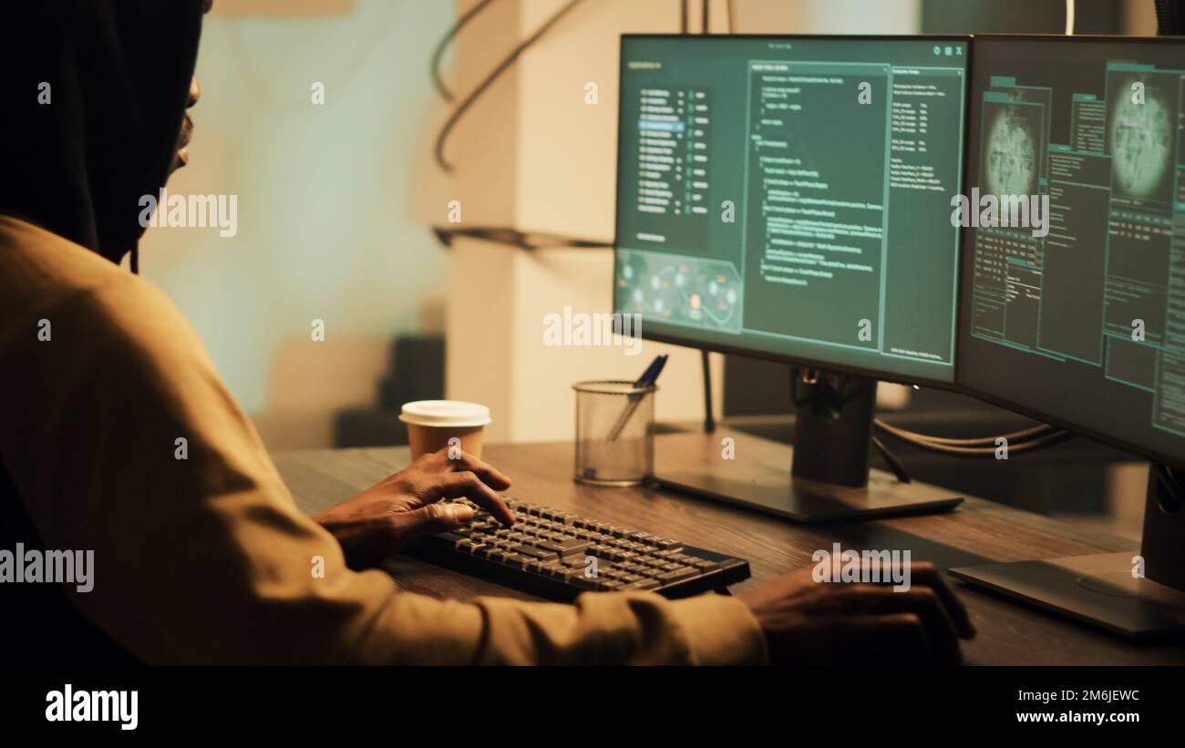 Young skilled thief doing illegal security breach late at night, working on cyberbullying to ...