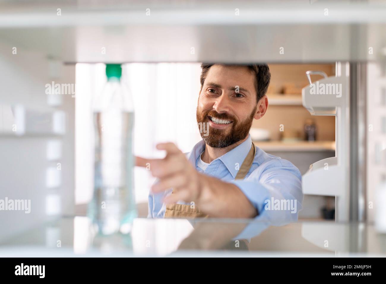 Smiling millennial caucasian bearded guy in apron opens door of empty ...