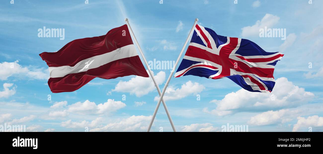 two crossed flags Great Britain and Latvia waving in wind at cloudy sky ...