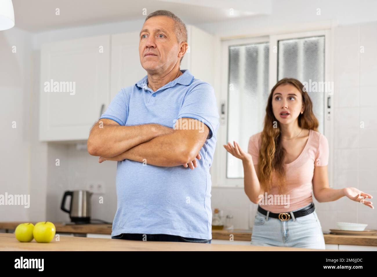 Adult daughter scolds an elderly father while he is preparing dinner in ...