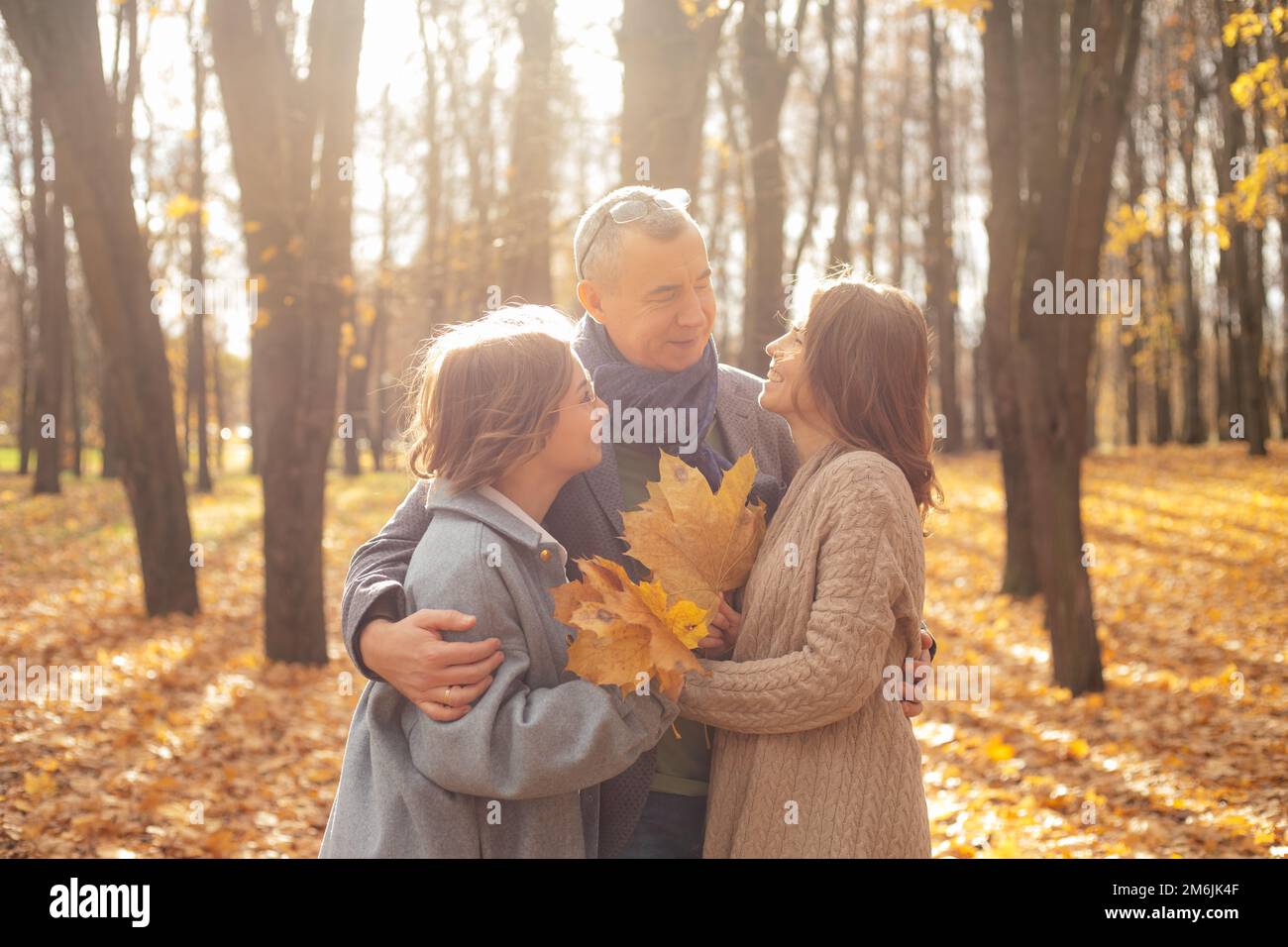 Portrait of loving family embracing, standing among trees in park ...