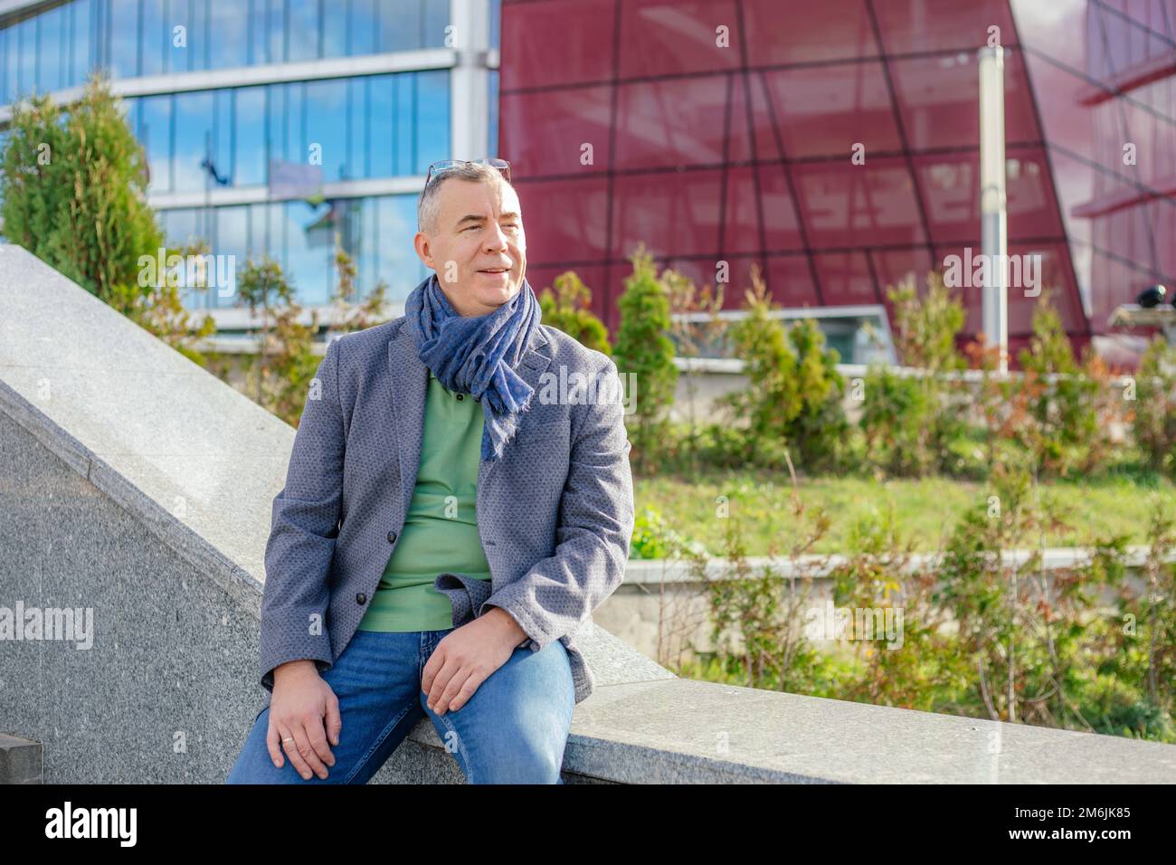 Portrait of cheerful middle-aged man sitting on concrete parapet near ...