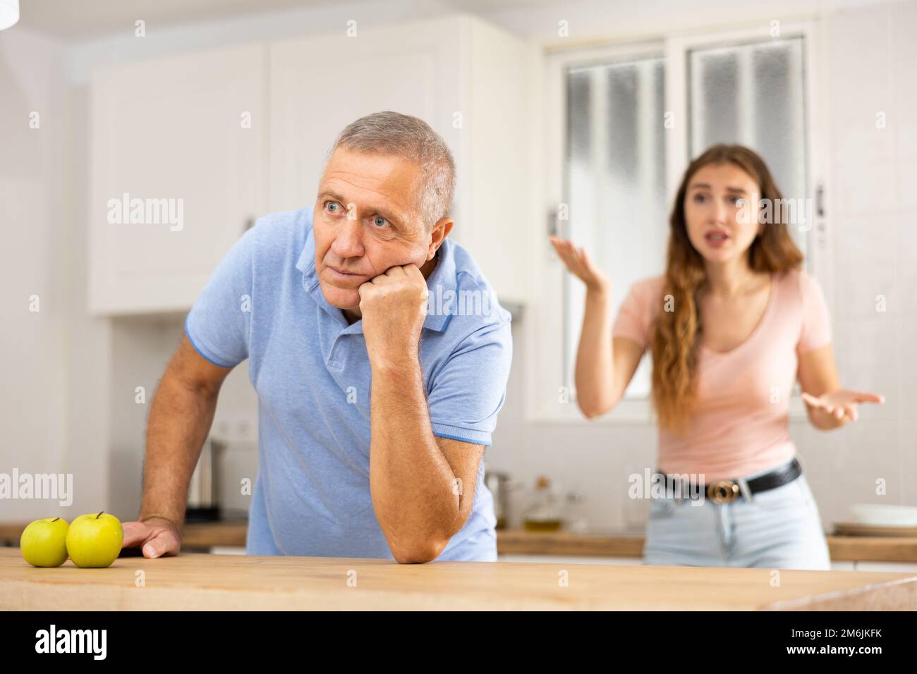 Adult daughter scolds an elderly father while he is preparing dinner in ...