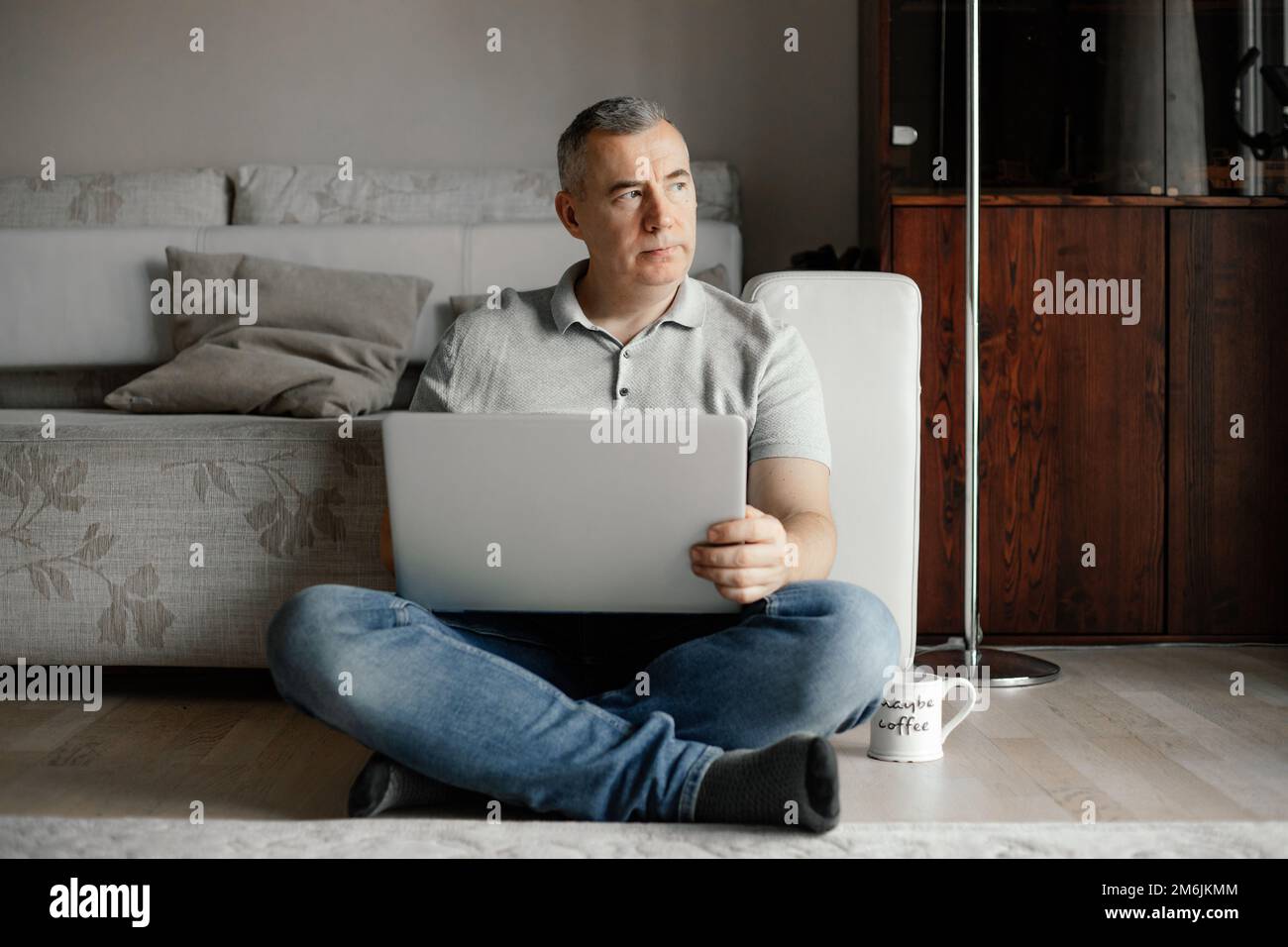 Portrait of thoughtful middle-aged man sitting with crossed legs near ...