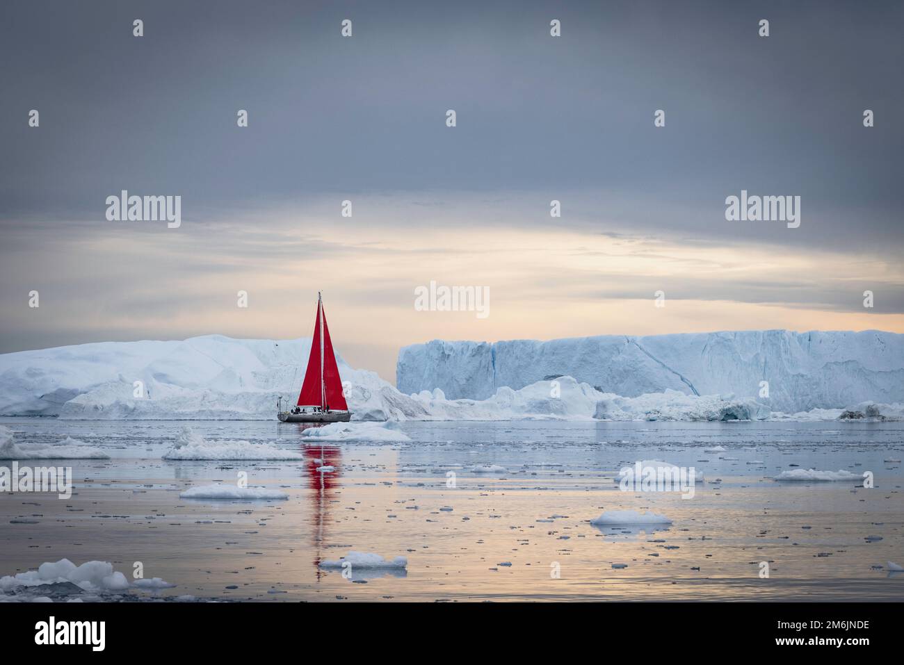 sailboat with red sails sailing between huge icebergs Stock Photo - Alamy