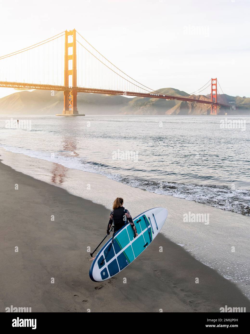 Woman carrying paddleboard walking towards Golden Gate Bridge Stock ...
