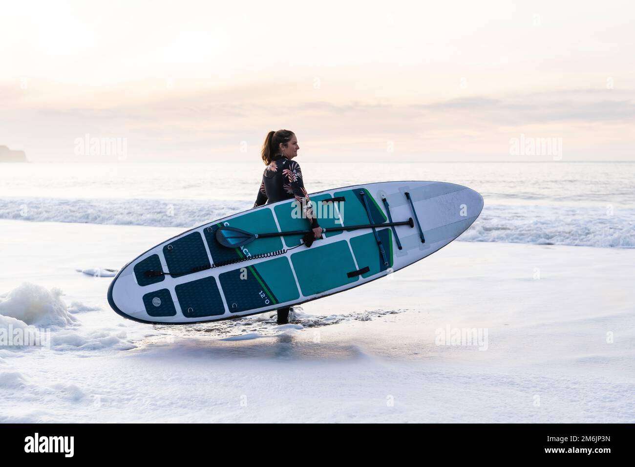 Woman carrying paddleboard on shore at sunset Stock Photo - Alamy