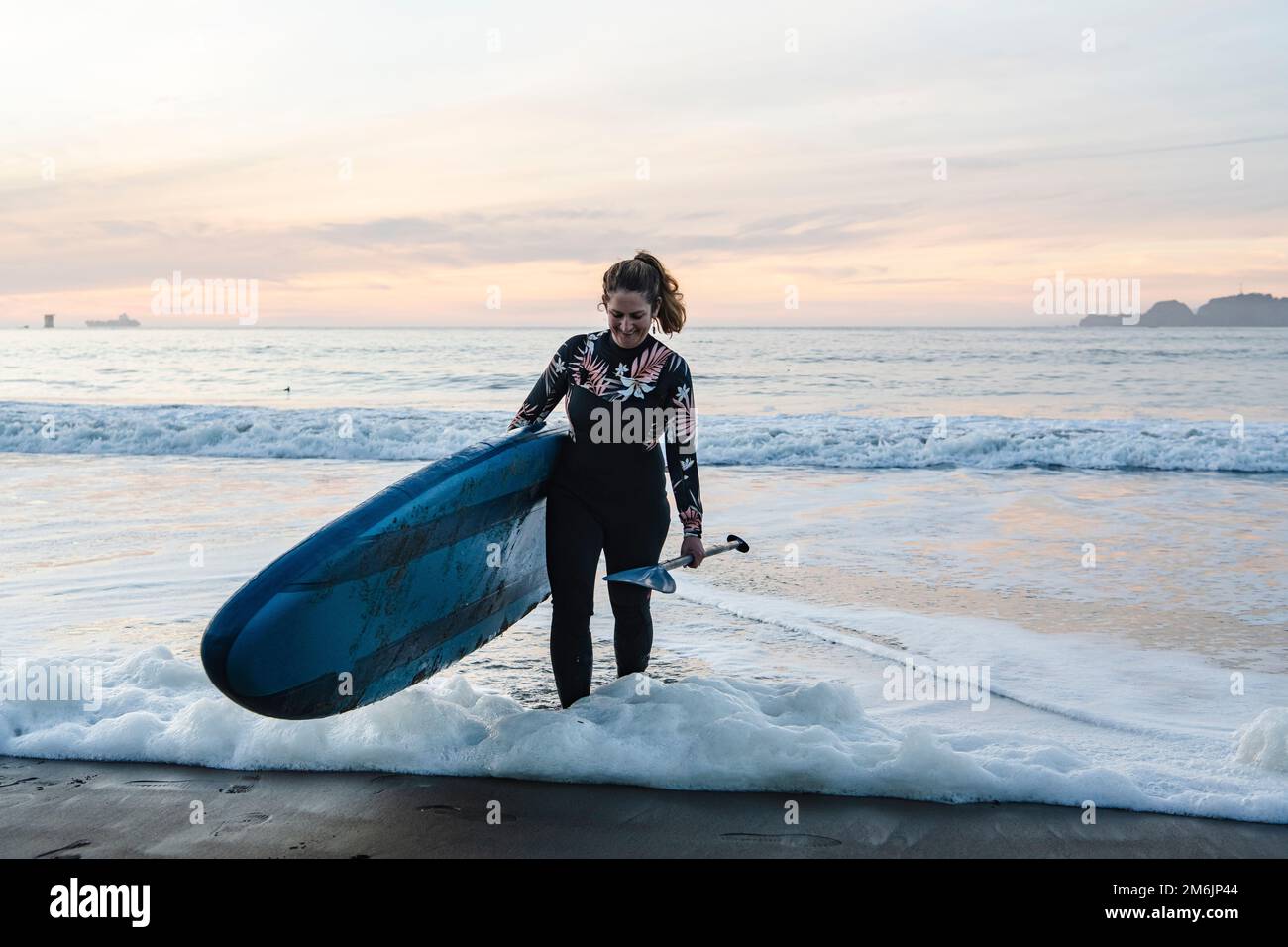 woman carrying paddleboard and oar walking on shore during sunset Stock ...
