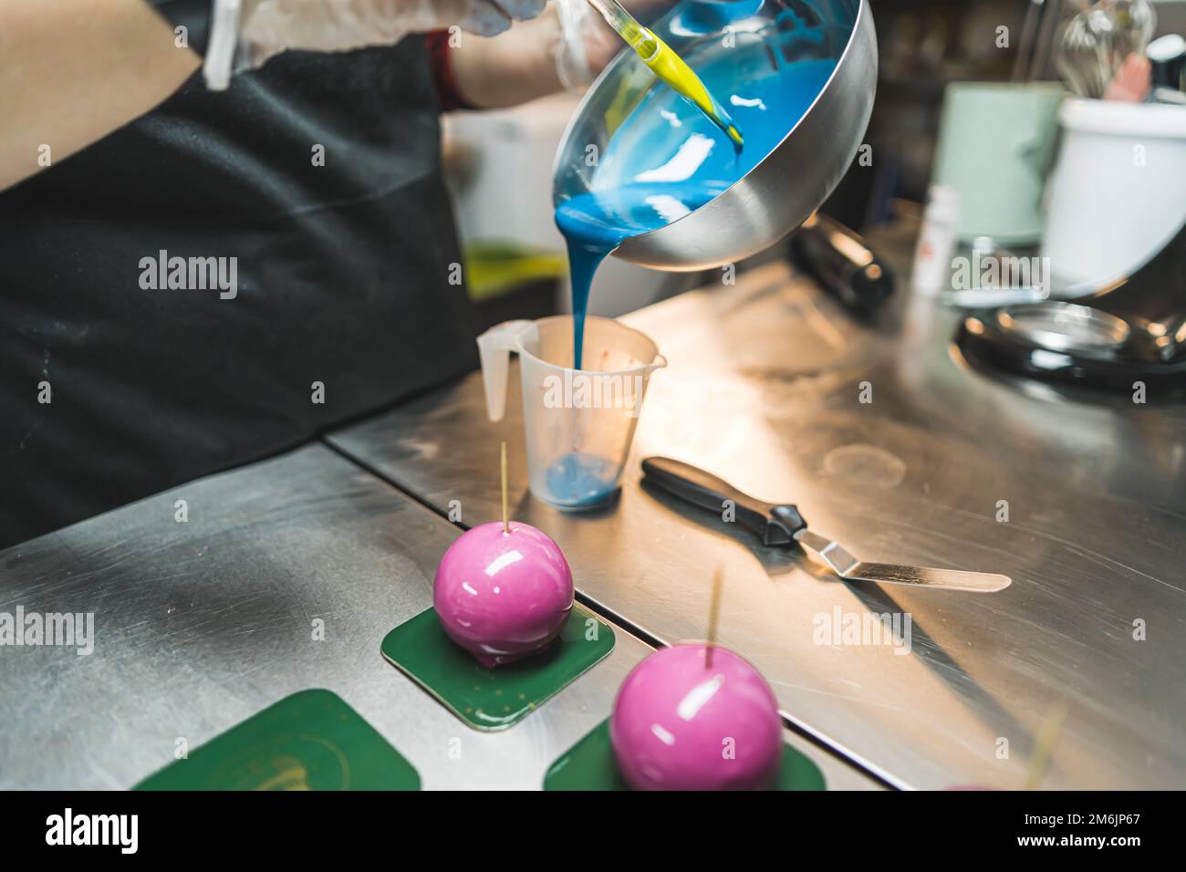 A baker wearing transparent gloves and black apron pouring blue icing ...