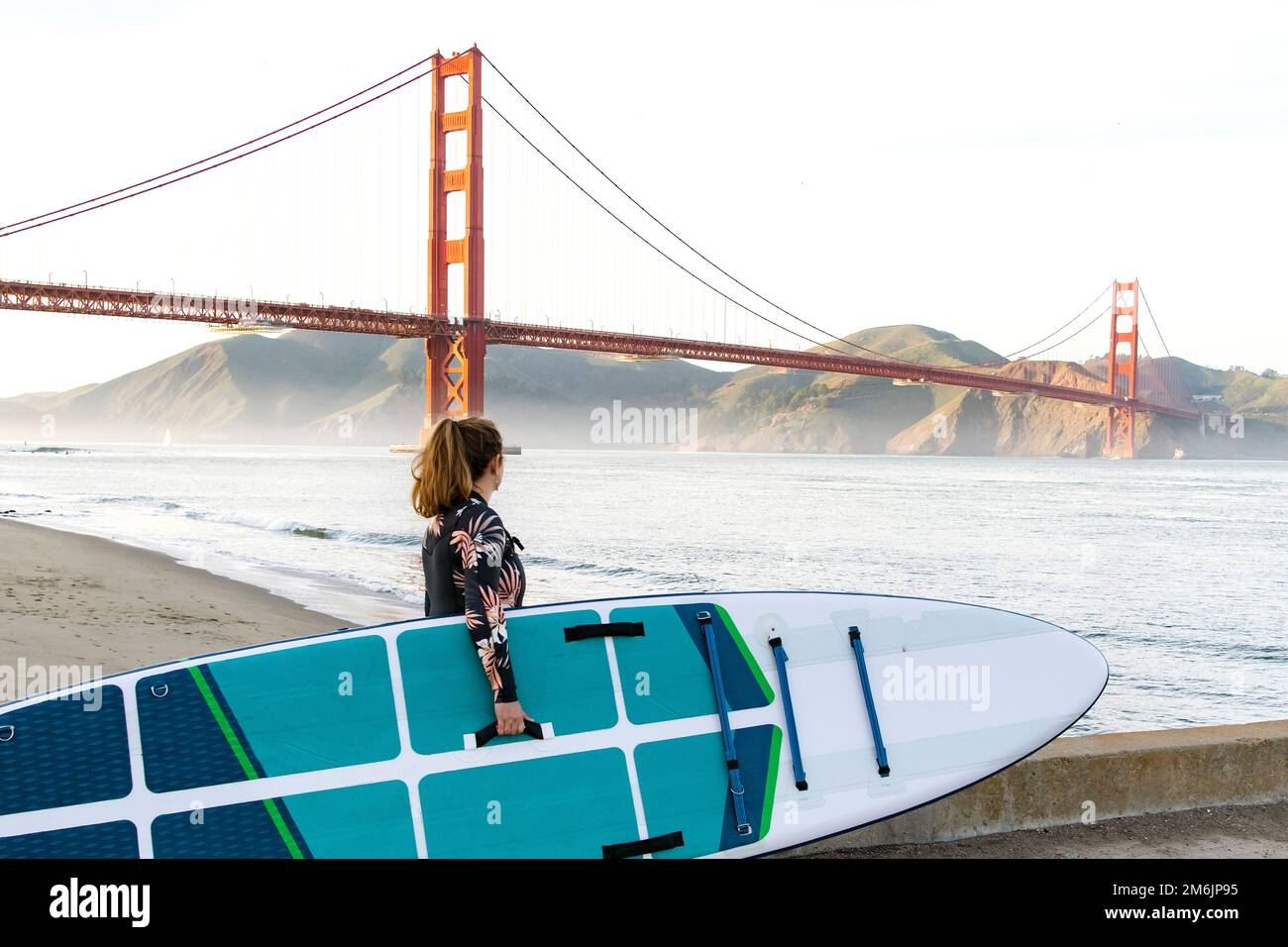 Side view of woman carrying paddleboard looking at Golden Gate Bridge ...