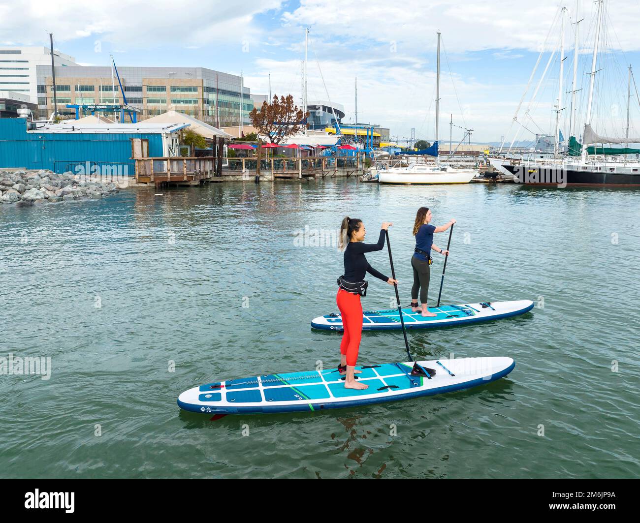 Side view of female friends paddleboarding at harbor in sea Stock Photo ...