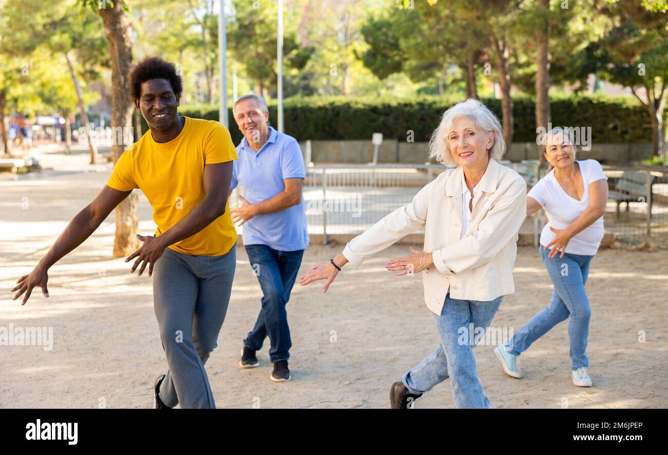 Positive mature women and men practicing vigorous dance movements in ...