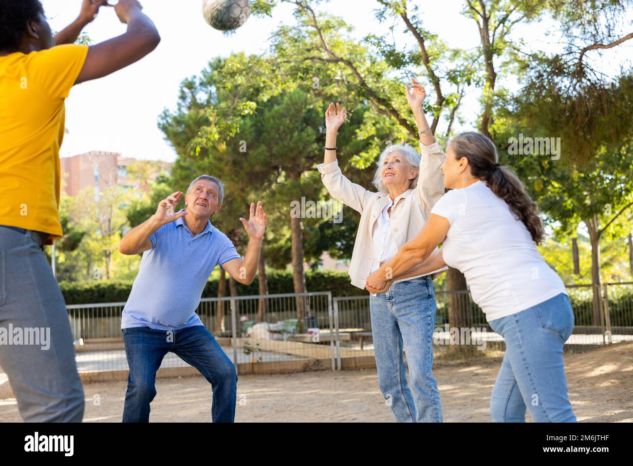 Joyful multiracial group of mature adult people playing volleyball game ...
