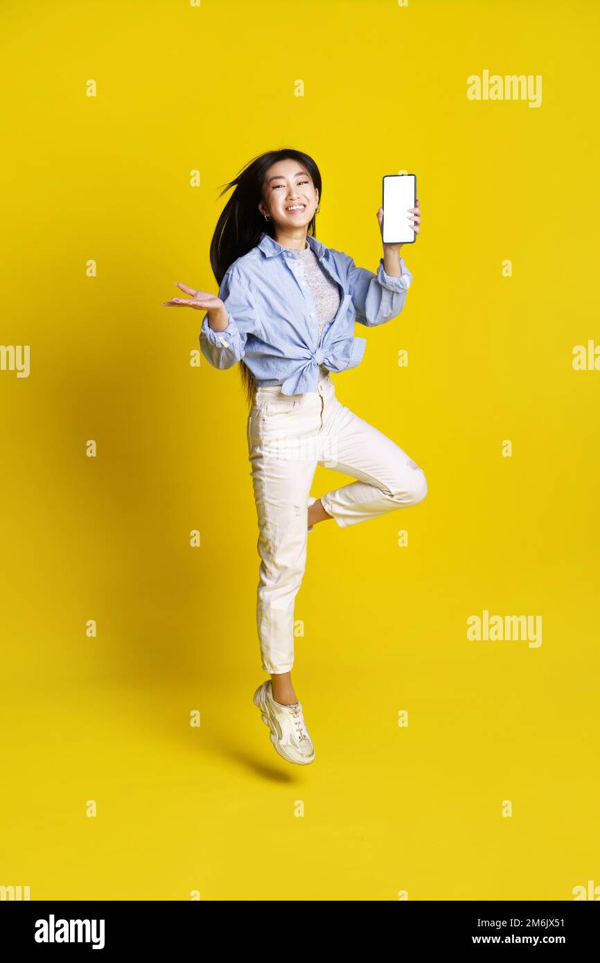 Happy asian girl jumping holding smartphone showing white screen mobile ...