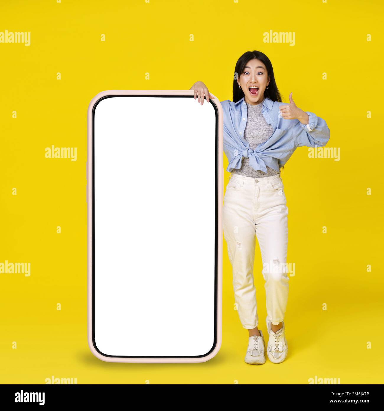 Excited asian girl gesturing thumb up leaned on giant, huge smartphone ...