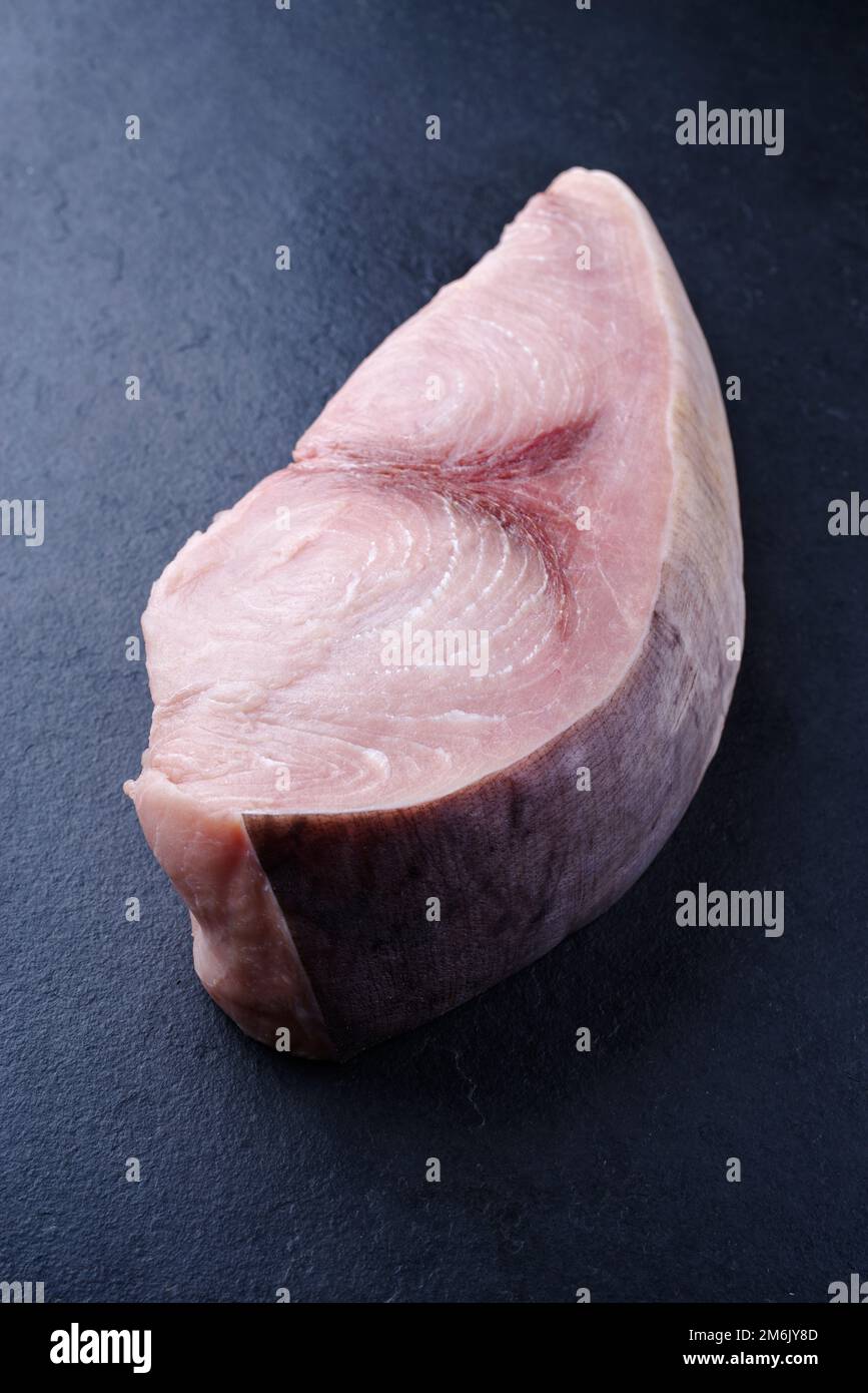 Raw swordfish steak offered as close-up on a black board with copy ...