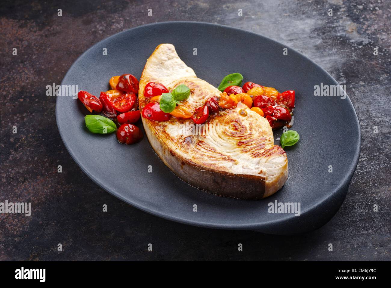 Fried swordfish steak with tomatoes and paprika served as close-up on a ...