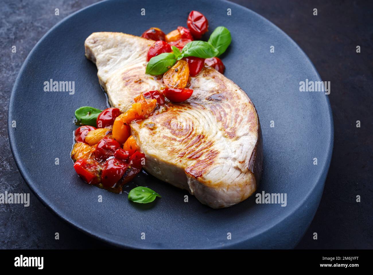 Fried swordfish steak with tomatoes and paprika served as close-up on a ...