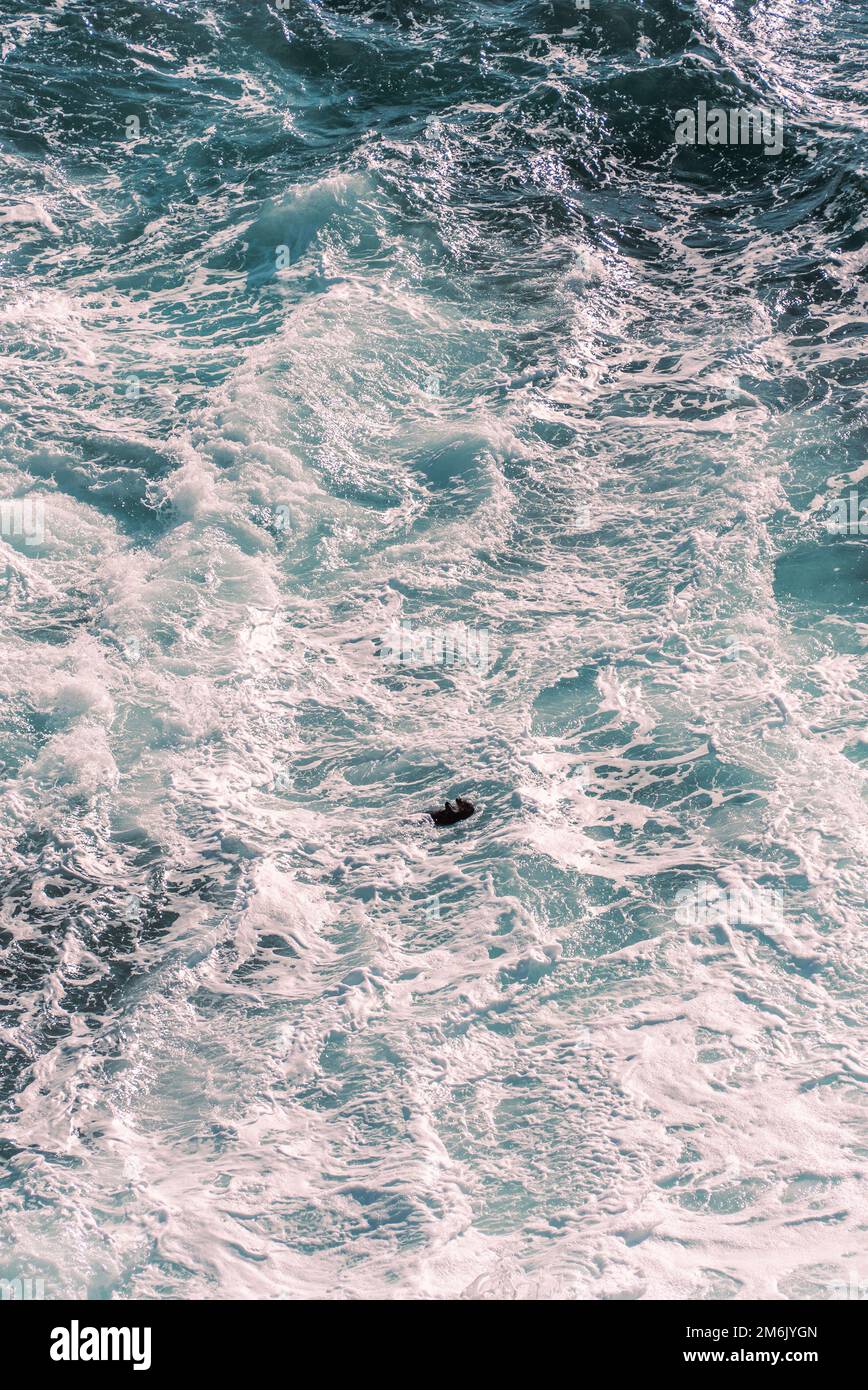 A vertical aerial of a rowing boat floating on the strong foamy waves ...