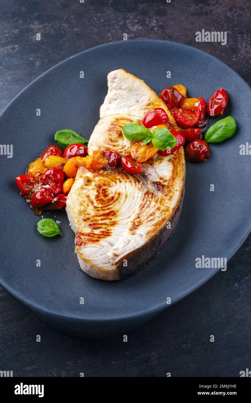 Fried swordfish steak with tomatoes and paprika served as close-up on a ...