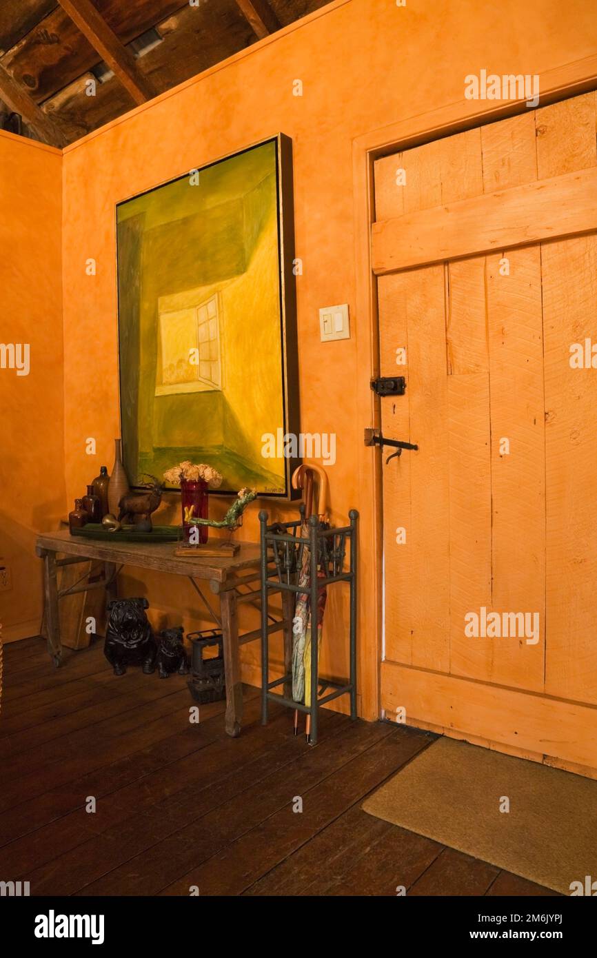 Painting on wall and small wooden table and umbrella rack next to ...