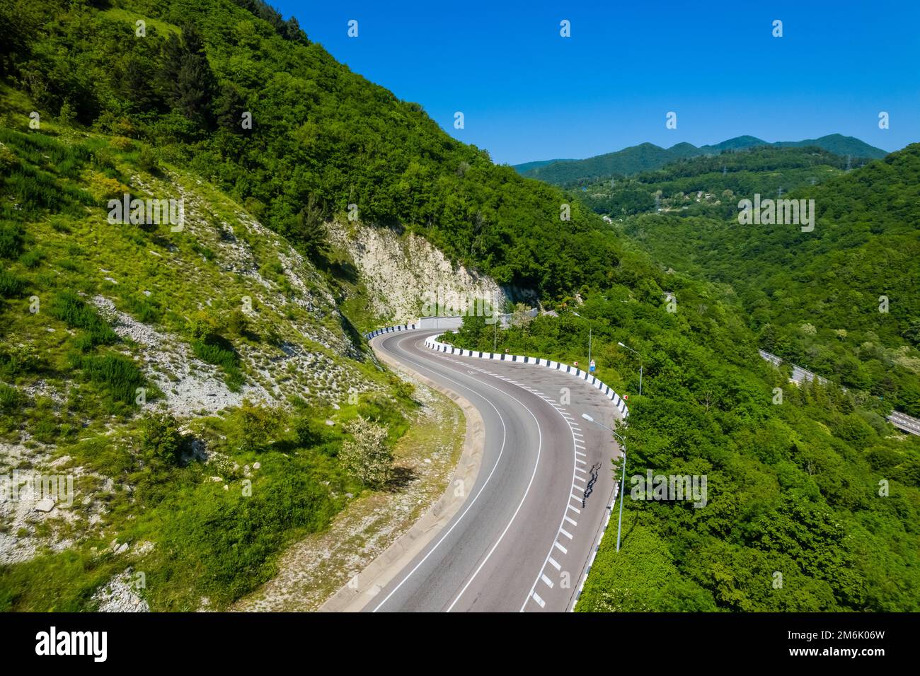 Asphalt road is meandering between blue sea and green mountains. Aerial ...