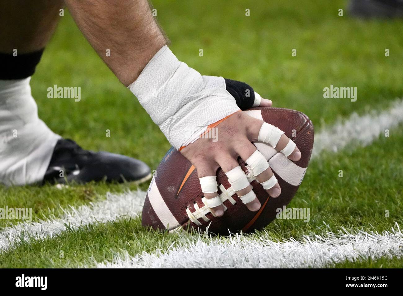 A football players hand with fingers taped up hold a football ready to ...