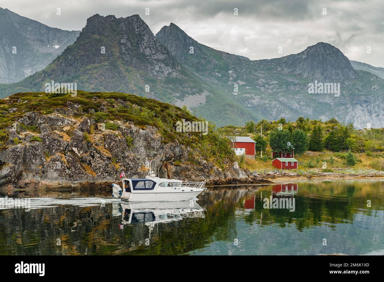 A small white fishing boat floats through the water along the rocks ...