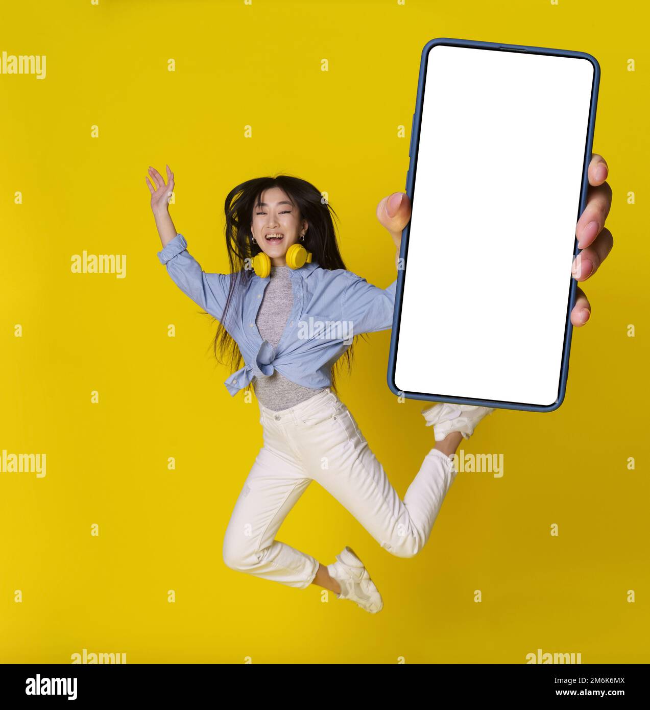 Happy jumping asian girl with smartphone in hand showing white screen ...