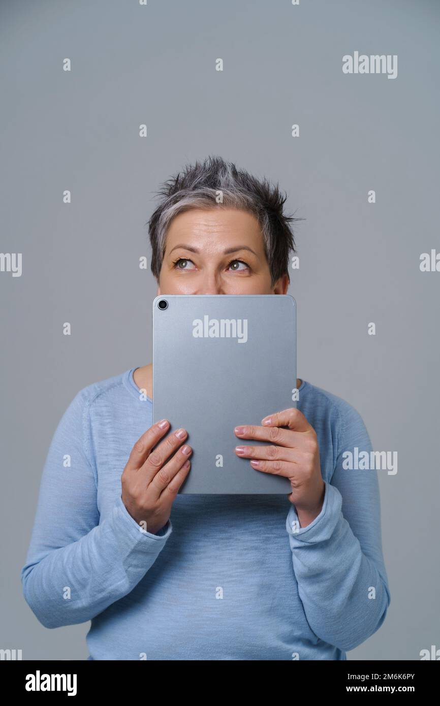 Thoughtful grey haired mature woman thinking hide face behind digital ...