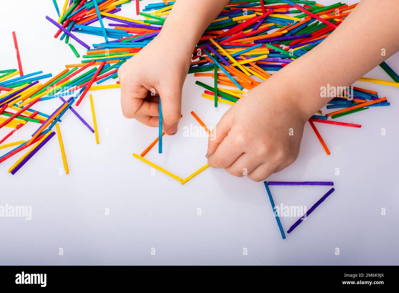 Kid making geometric shapes with colorful sticks on white background ...