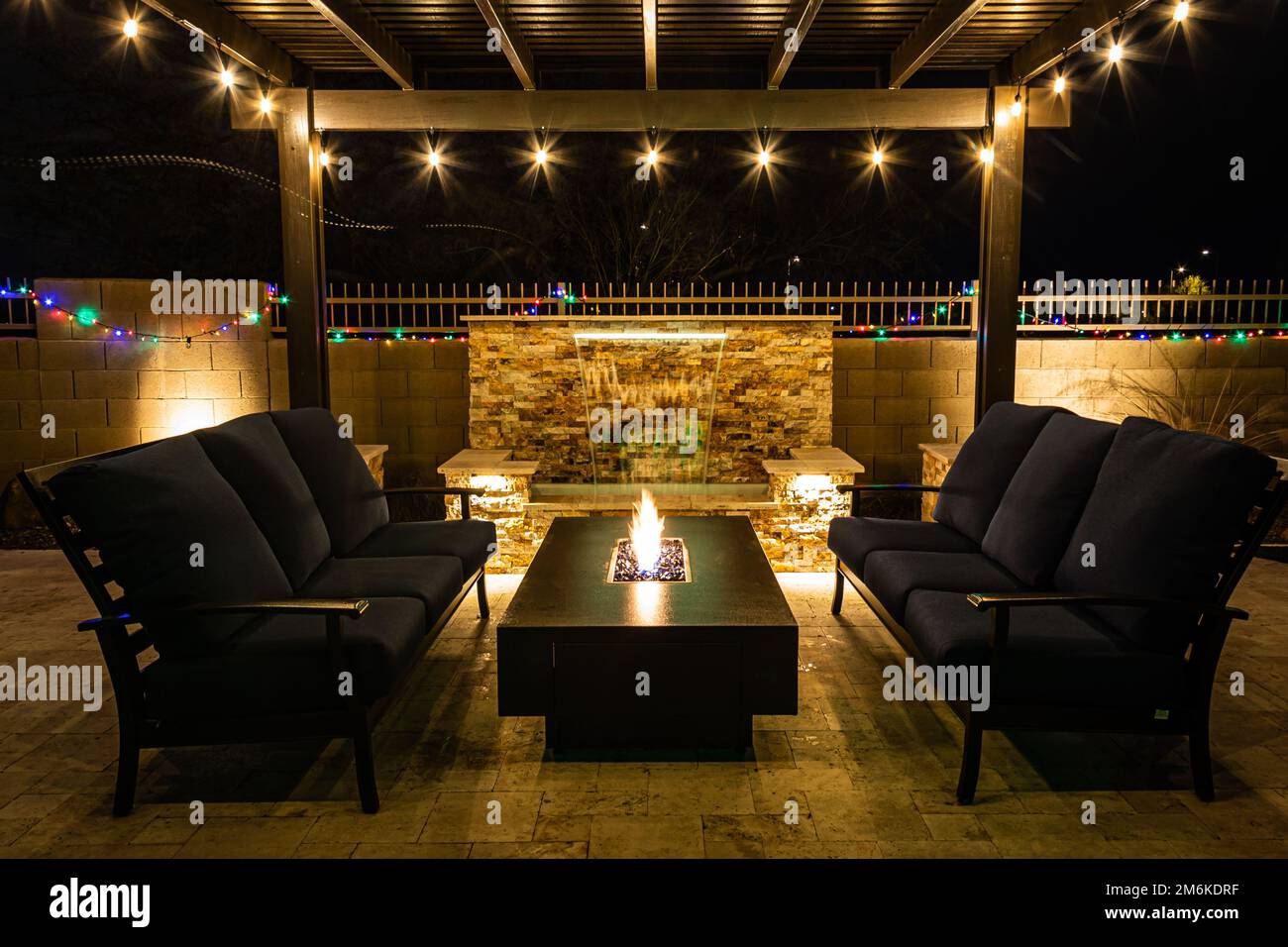 A resort style backyard at night with a waterfall, pergola, and a ...