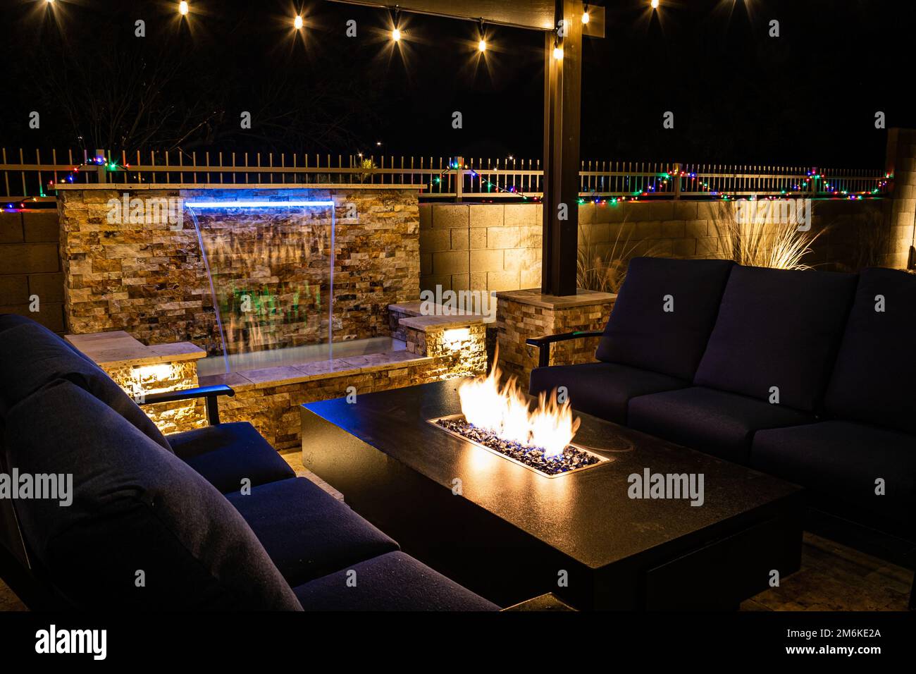 A resort style backyard at night with a waterfall, pergola, and a ...