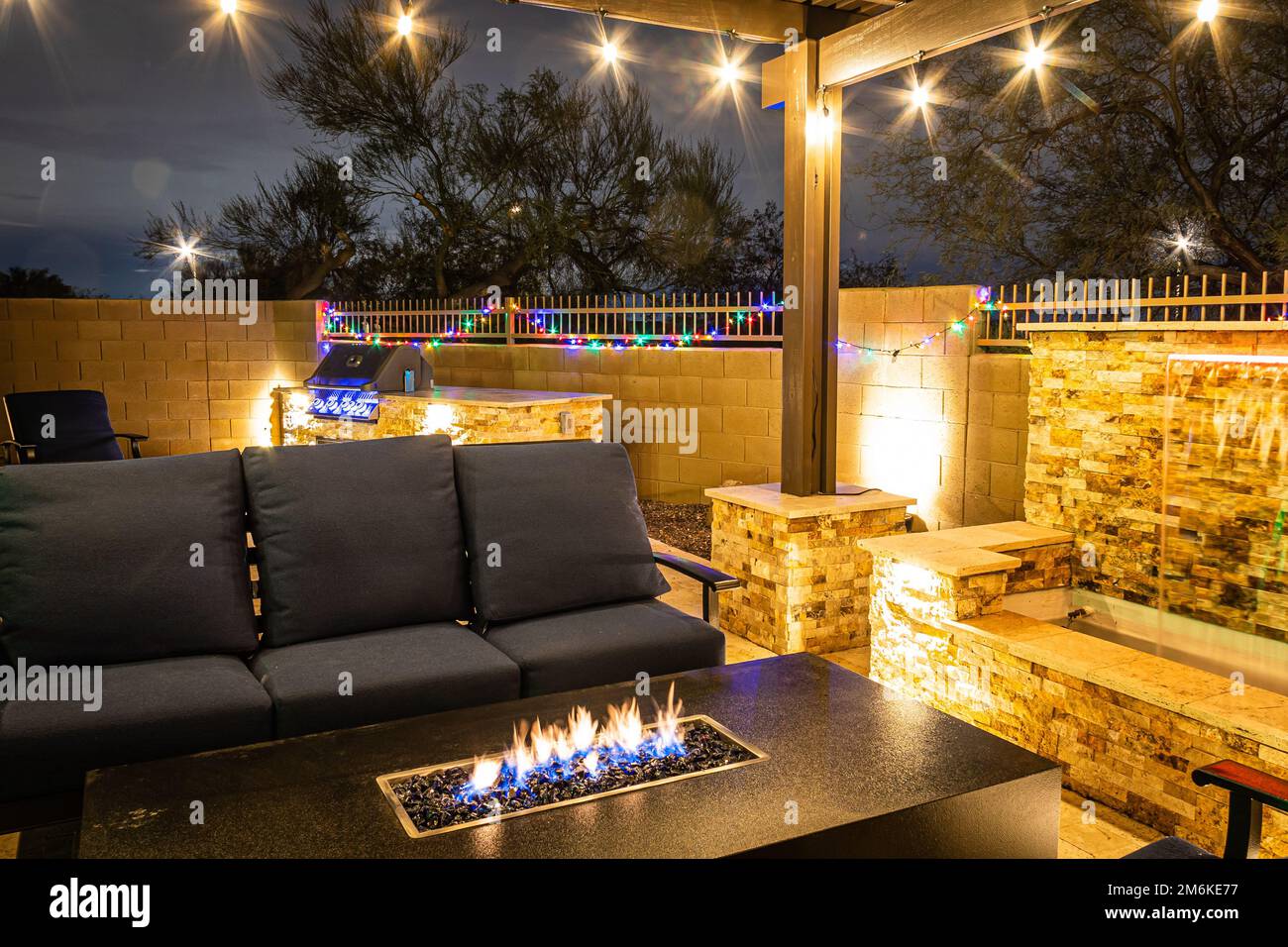 A resort style backyard at night with a waterfall, pergola, and a ...