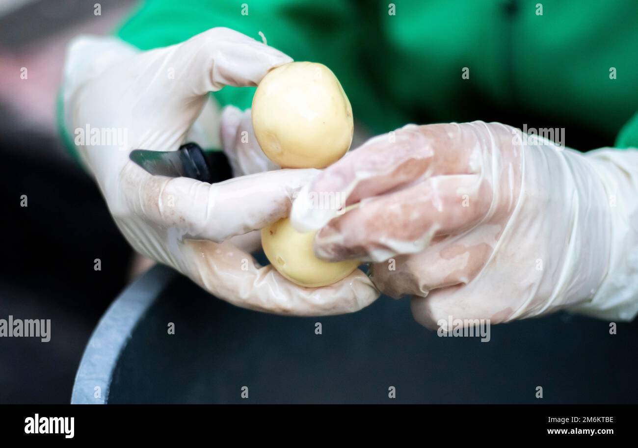 Woman's hands in white gloves peel raw new potatoes, close-up. Cleaning ...