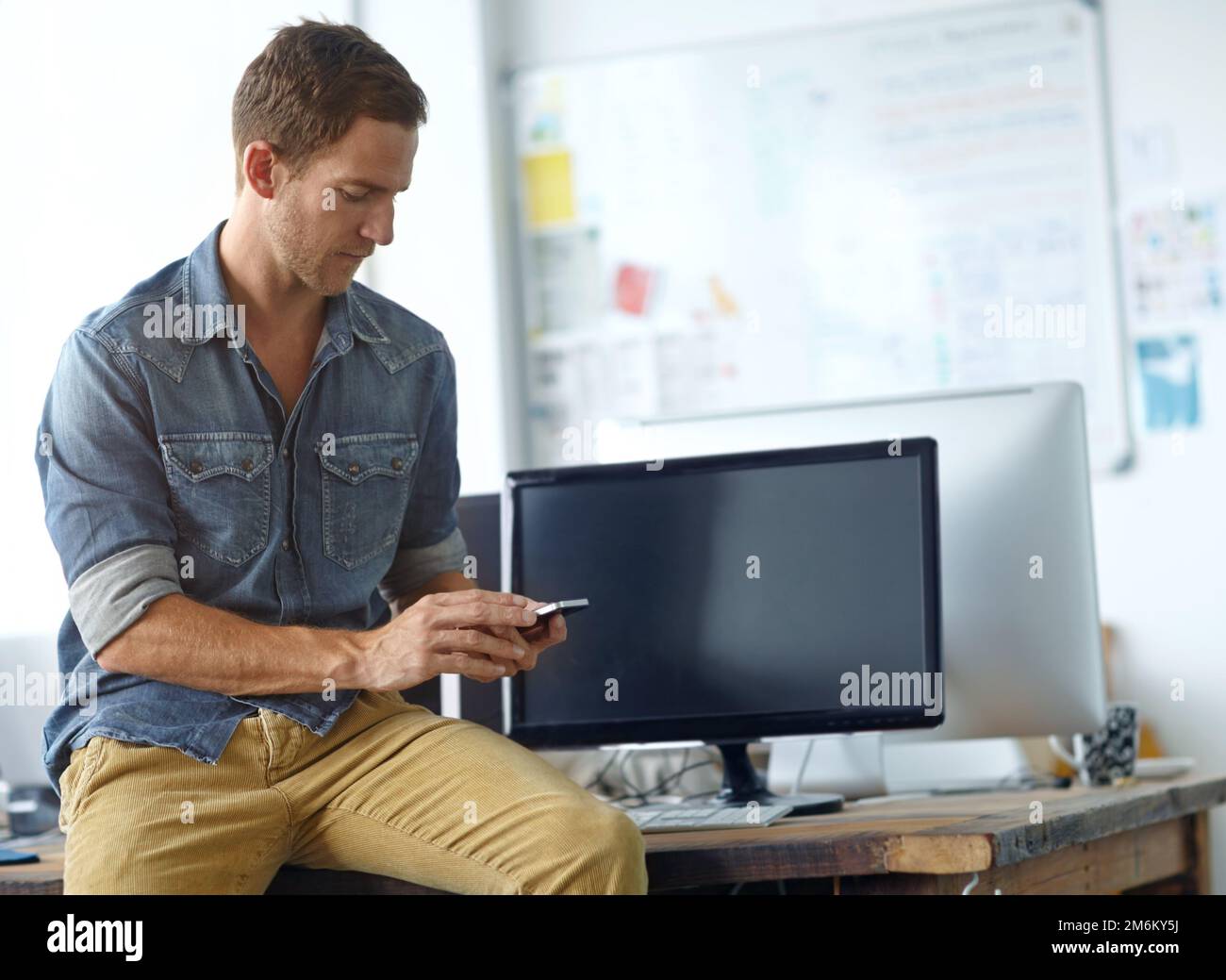 Casual working environment. A young man sitting on his desk at work ...