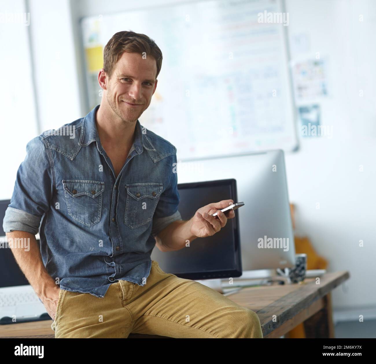 Taking a break to read his messages. A young man sitting on his desk at ...
