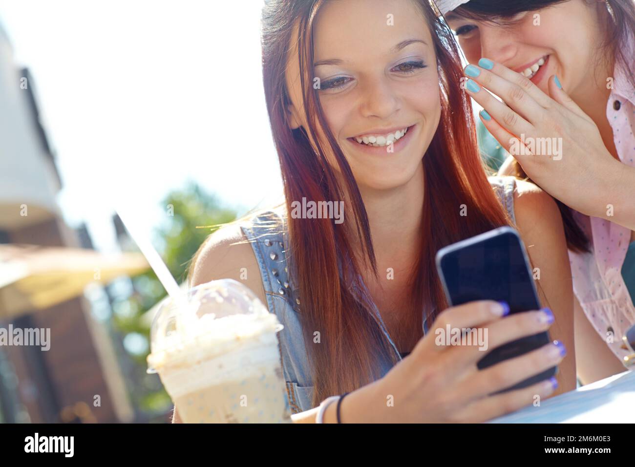 Sharing a naughty text. A teenage girl texting on a cellphone while her ...