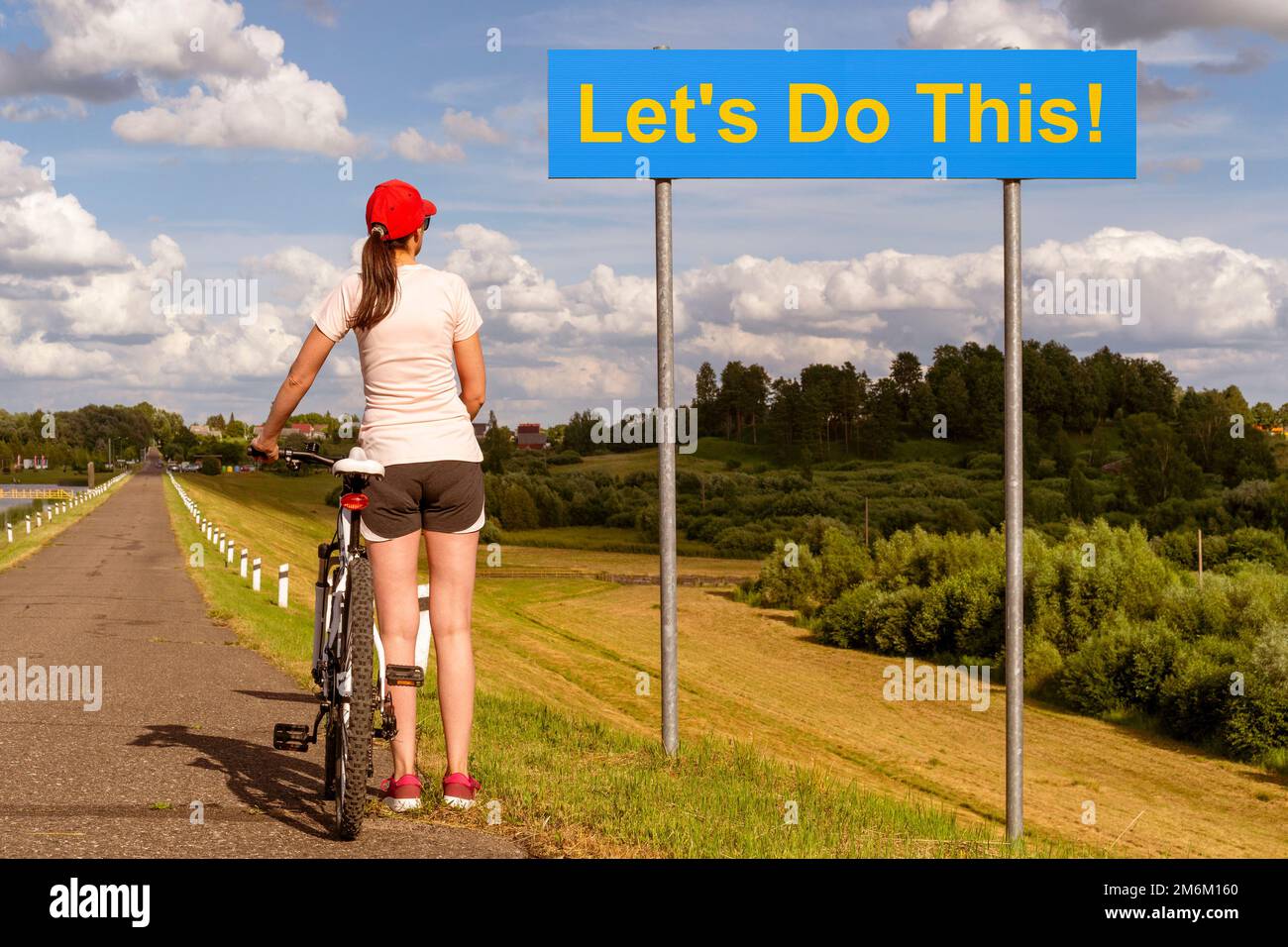 Young woman cyclist reads text Let's Do This! written on a highway road ...