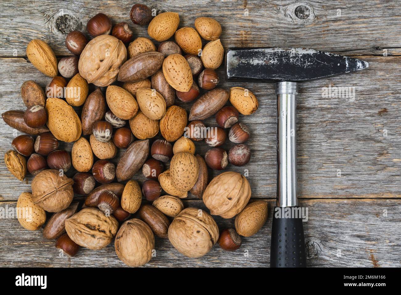Hammer and pile of various nuts on a wooden background Stock Photo - Alamy