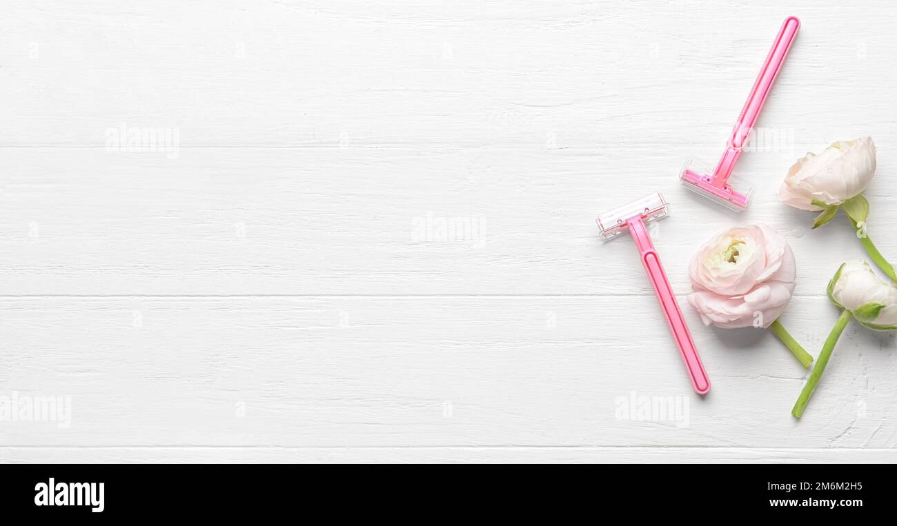 Safety shaving razors and ranunculus flowers on white wooden background ...