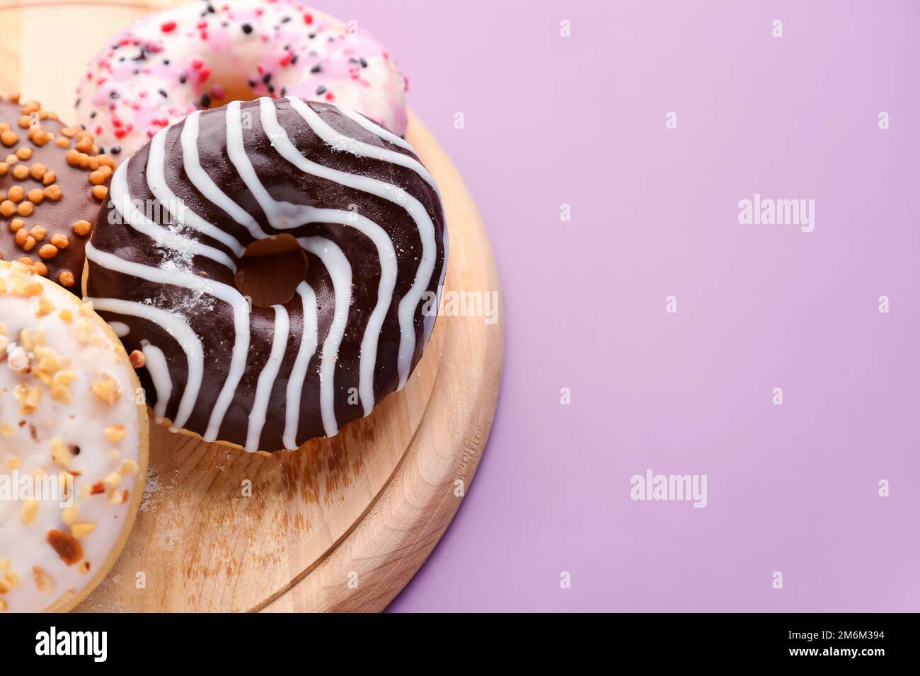 Wooden board with delicious donuts on lilac background, closeup Stock ...