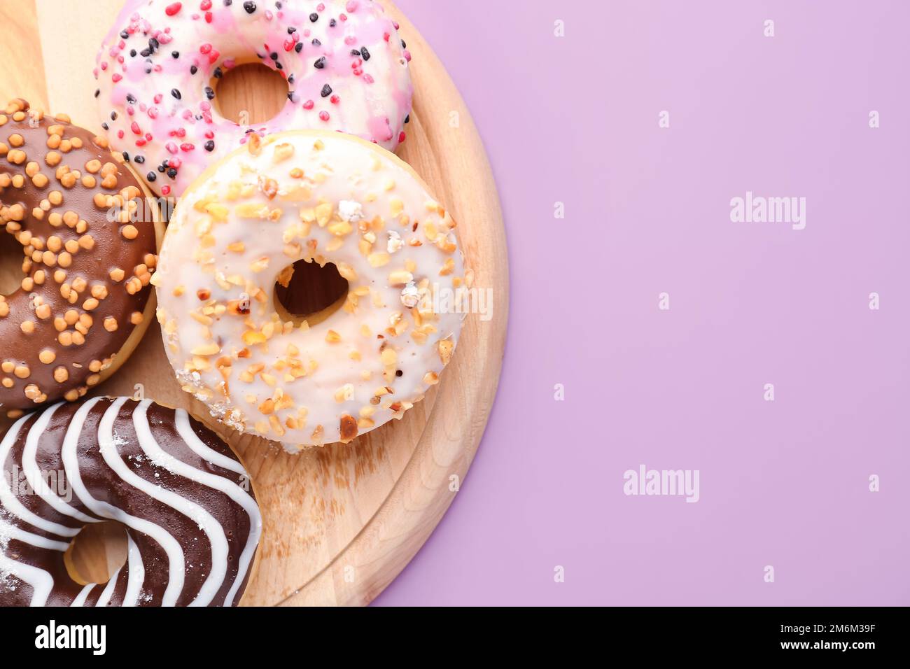 Wooden board with delicious donuts on lilac background, closeup Stock ...